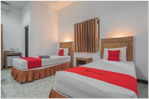 Quarto de hotel com duas camas, cada uma com colcha vermelha e branca, cabeceiras de madeira e mesas de cabeceira com luminárias.