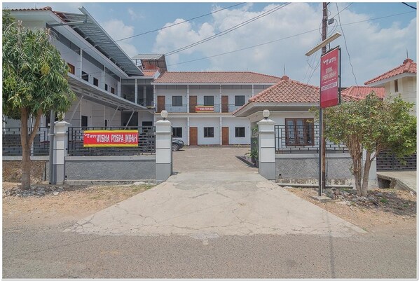 Um edifício com entrada protegida por portão, uma placa de identificação e um painel solar em um poste.