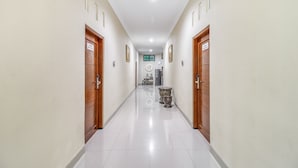 Um corredor comprido e estreito com paredes brancas e chão de azulejos brilhantes, que leva a um quarto com uma janela grande e uma mesa redonda.