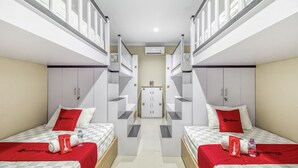 Quarto de hotel com duas camas, cada uma com colcha vermelha e almofadas combinando, um minibar e vista para o corredor.
