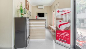 Uma área de recepção de hotel com balcão de madeira, um refrigerador, uma TV de tela plana e um anúncio da RedDoorz.