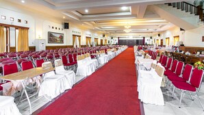 Uma sala de banquetes com fileiras de mesas e cadeiras, um tapete vermelho e uma escadaria.