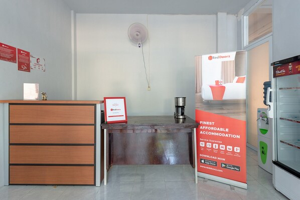 Uma área de recepção com uma mesa de madeira, uma máquina de café e um anúncio da RedDoorz.