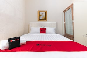 Quarto de hotel com cama, manta vermelha, travesseiro, quadro na parede e porta com janela.