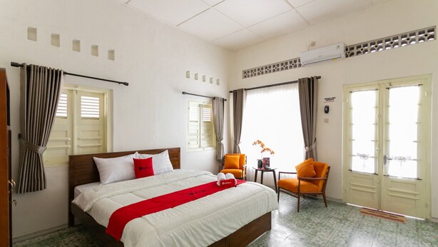 Quarto de hotel com uma cama, uma cadeira, uma mesa pequena e uma janela com cortinas.