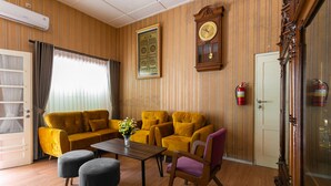 Quarto com sofá, pufes, uma mesa com um vaso, relógio e extintor de incêndio.