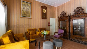 Um quarto com painéis de madeira, um relógio grande, um armário de madeira com portas de vidro e duas poltronas.