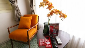 Quarto de hotel com uma cadeira de madeira, uma mesa com controle remoto, um vaso com flores e uma placa indicando horário de silêncio.