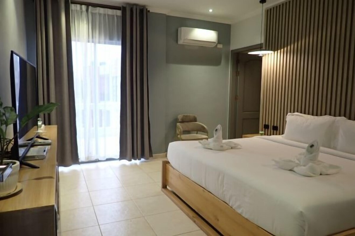 Quarto de hotel com uma cama grande, uma escrivaninha com computador, uma cadeira e uma televisão.