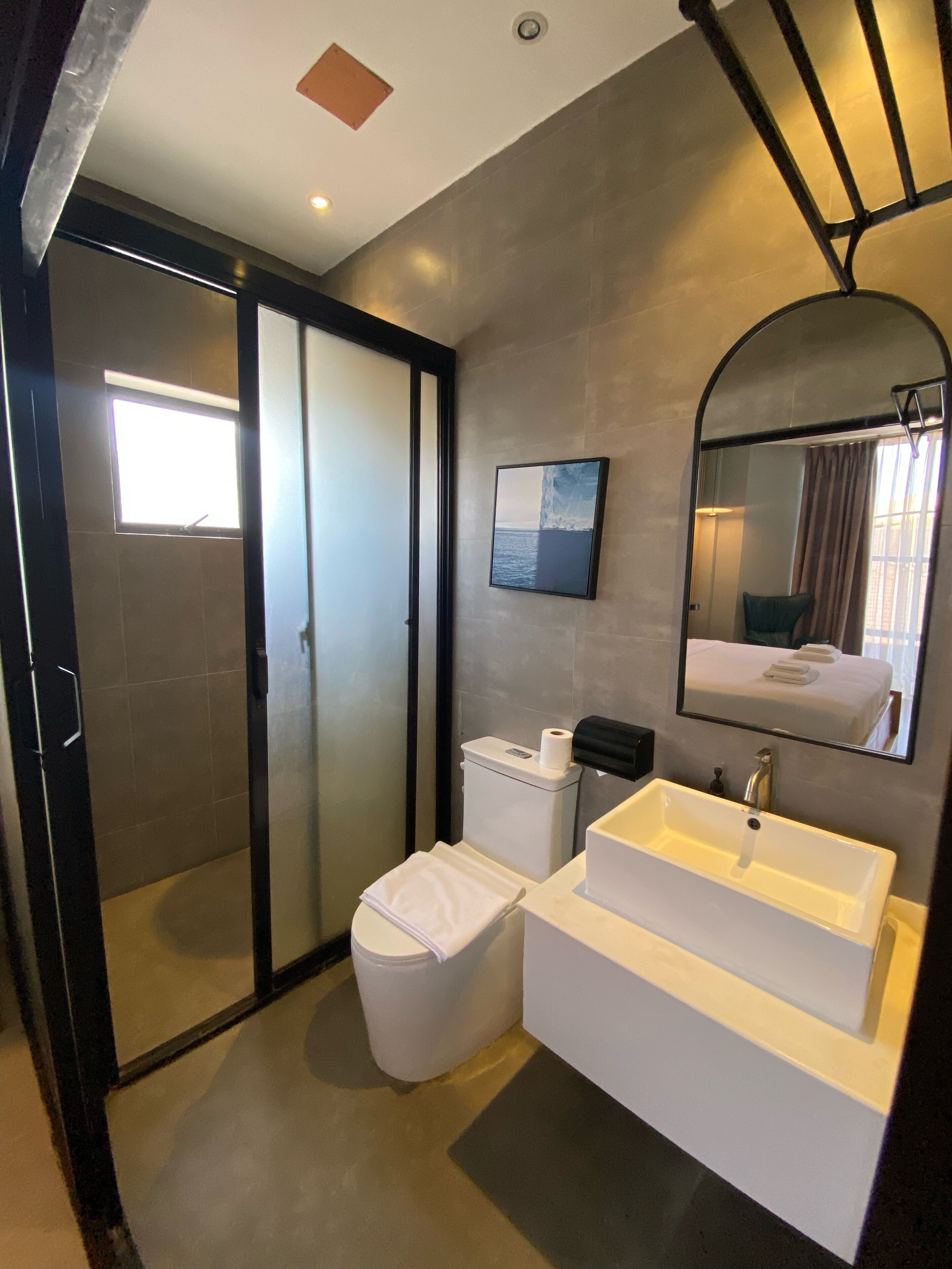 Uma casa de banho moderna com chuveiro em cabine de vidro, sanita, lavatório e espelho.