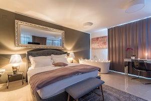 Quarto de hotel moderno com uma cama grande, luminárias de cabeceira, toucador iluminado, escrivaninha e um espelho amplo.