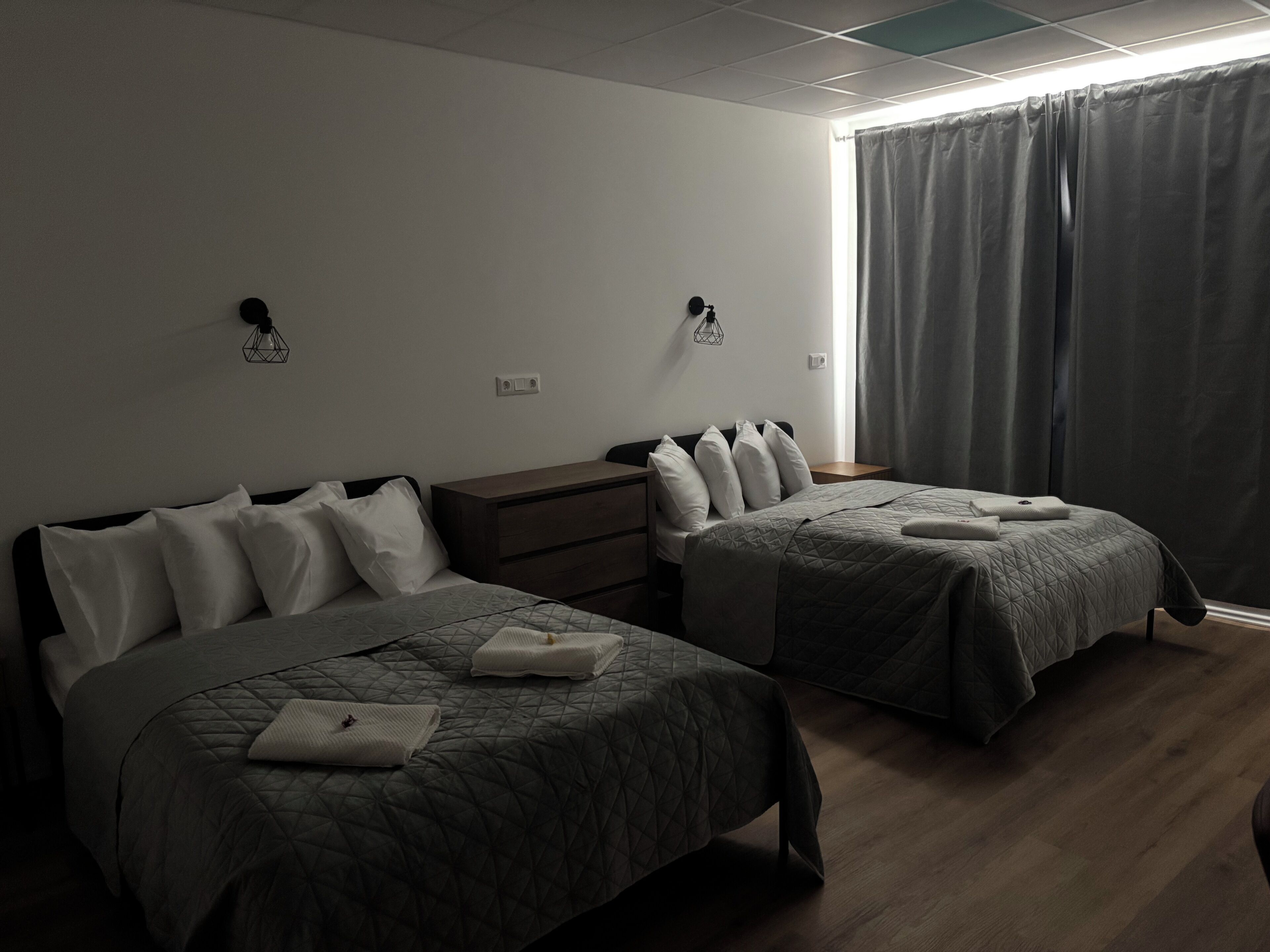 Quarto de hotel com duas camas, uma cômoda de madeira e uma janela com cortinas.