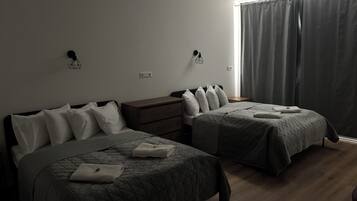 Quarto de hotel com duas camas, uma cômoda de madeira e uma janela com cortinas.