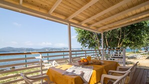 Uma área de refeições coberta ao ar livre, com uma mesa posta para dois, com vista para um corpo d'água e uma paisagem montanhosa.