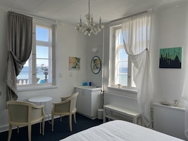 Quarto com cama, escrivaninha, cadeira, mesa pequena e janela com cortinas.