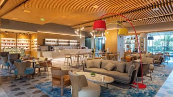 Um lobby de hotel moderno com bar, áreas de estar e vista para o exterior.