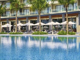 Um hotel com piscina, espreguiçadeiras, guarda-sóis e palmeiras.