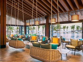 Espaço de descanso com mobiliário de vime, vista para a piscina e teto de madeira.