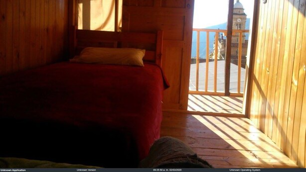 Quarto de cabana de madeira com cama, janela com cortinas e varanda com vista para um edifício.