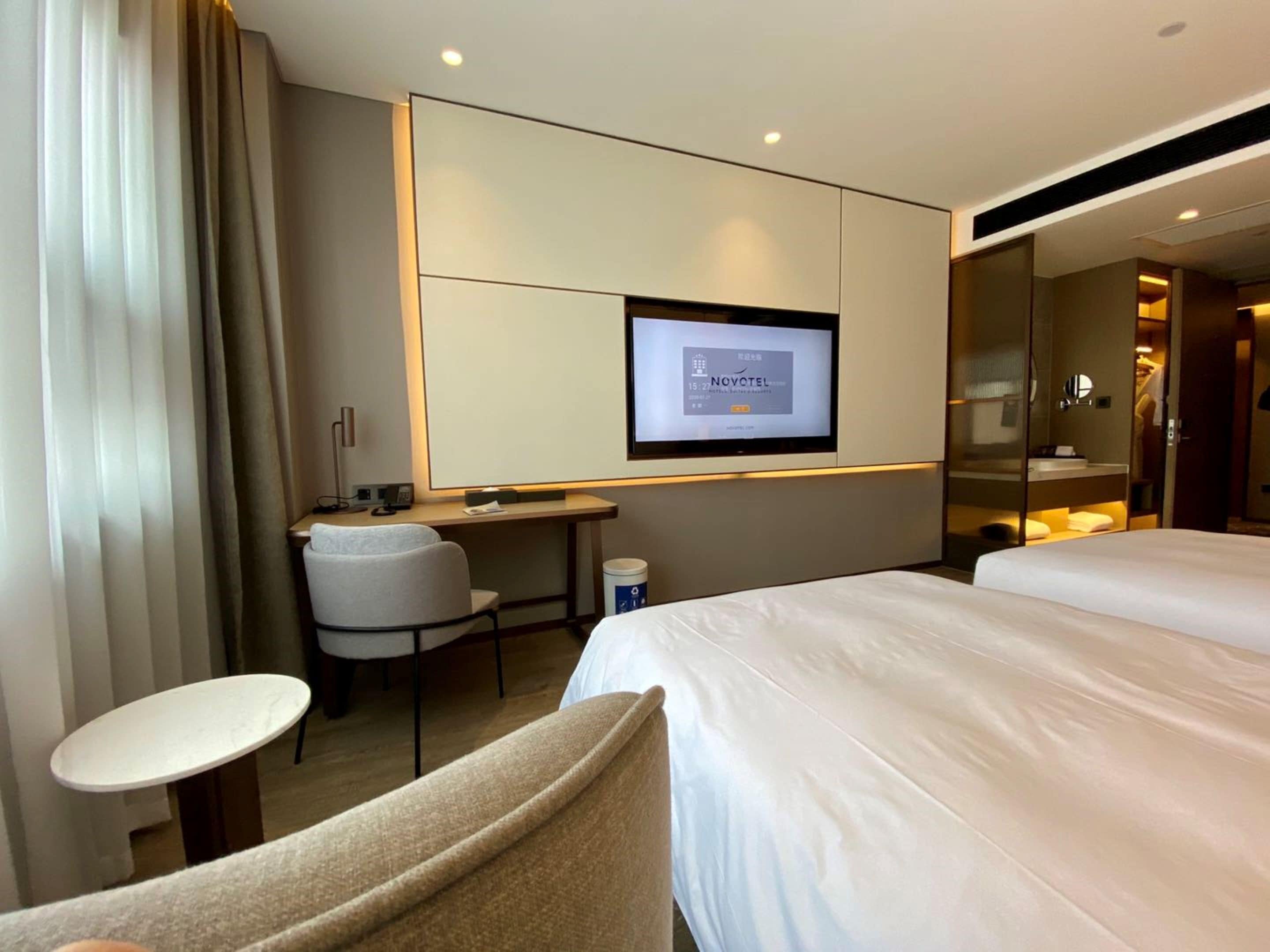 Quarto de hotel com cama, escrivaninha, cadeira, televisão e minibar.