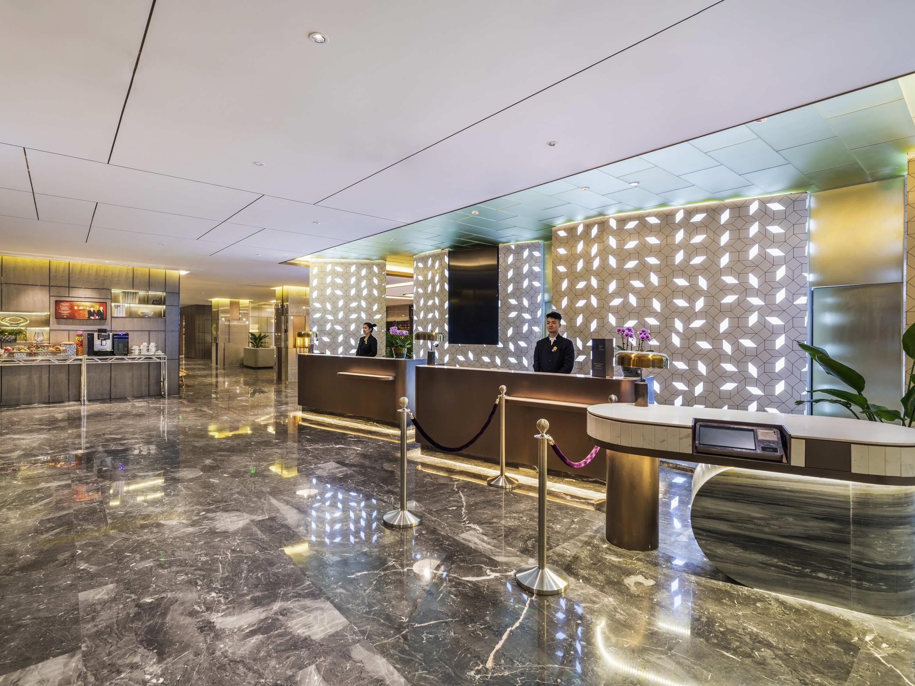 Uma área de recepção de hotel com piso de mármore, balcão de atendimento e design moderno na parede.