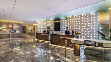Uma área de recepção de hotel com piso de mármore, balcão de atendimento e design moderno na parede.
