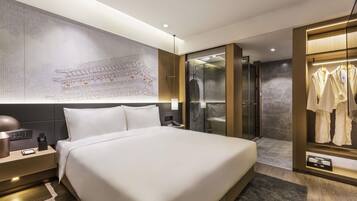 Quarto de hotel moderno com uma cama grande, mesa de cabeceira, mapa fixado na parede, closet espaçoso e área de chuveiro.