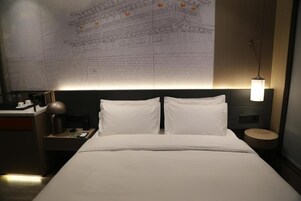 Quarto de hotel com uma cama, mesa de cabeceira, abajur e parede com um mapa.