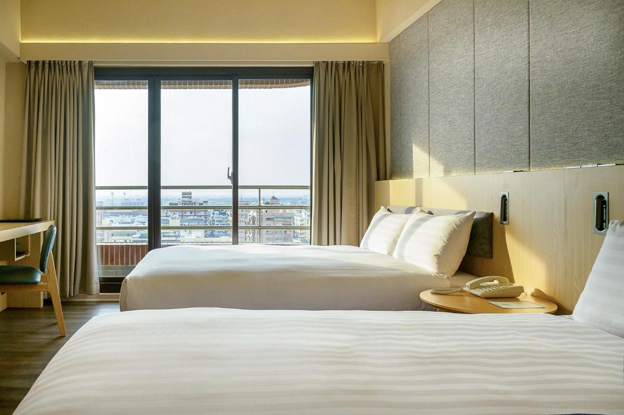 Quarto de hotel com duas camas, uma escrivaninha e vista para a cidade.