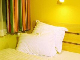 Cama com roupa de cama branca, cabeceira de madeira e parede amarela.
