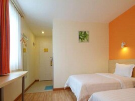 Quarto de hotel com duas camas, uma secretária pequena, uma porta e um candeeiro fixo na parede.