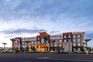 Um hotel Hampton Inn & Suites com design moderno, apresentando uma entrada imponente, vários andares e uma área de estacionamento.