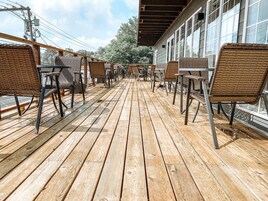 Um deck de madeira com cadeiras e mesas de vime, com vista para um edifício com grandes janelas.