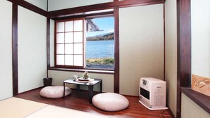 Quarto com piso de tatame, uma mesinha baixa com uma pequena planta, aquecedor e janela com vista para uma ponte e água.