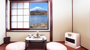 Quarto com vista para montanha e lago, uma pequena mesa com um arranjo de flores, e um ar condicionado branco.