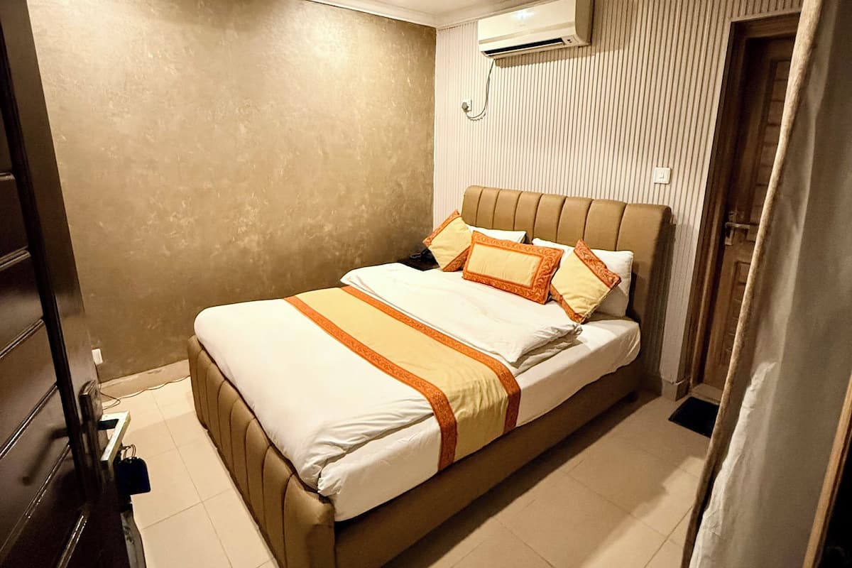 Quarto com cama, ar condicionado, ventoinha no teto e porta.