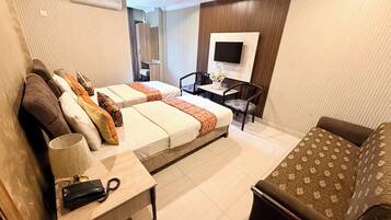 Quarto de hotel com duas camas, um sofá, uma televisão, uma mesa e uma cadeira.