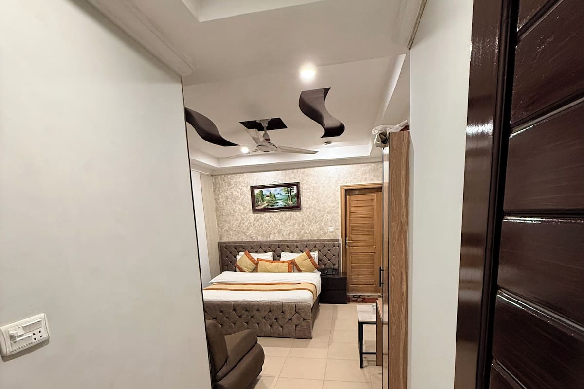 Um corredor estreito que dá para um quarto com uma cama, uma mesa de cabeceira e uma porta de madeira.