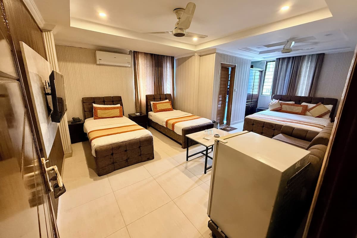 Quarto de hotel com três camas, televisão, ventoinha no teto e ar condicionado.