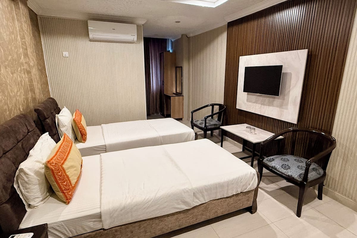 Quarto de hotel com duas camas, televisão fixada na parede, mesa pequena com cadeiras e aparelho de ar condicionado.
