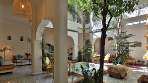Um espaço amplo e coberto com uma fonte central, rodeado por assentos e plantas.