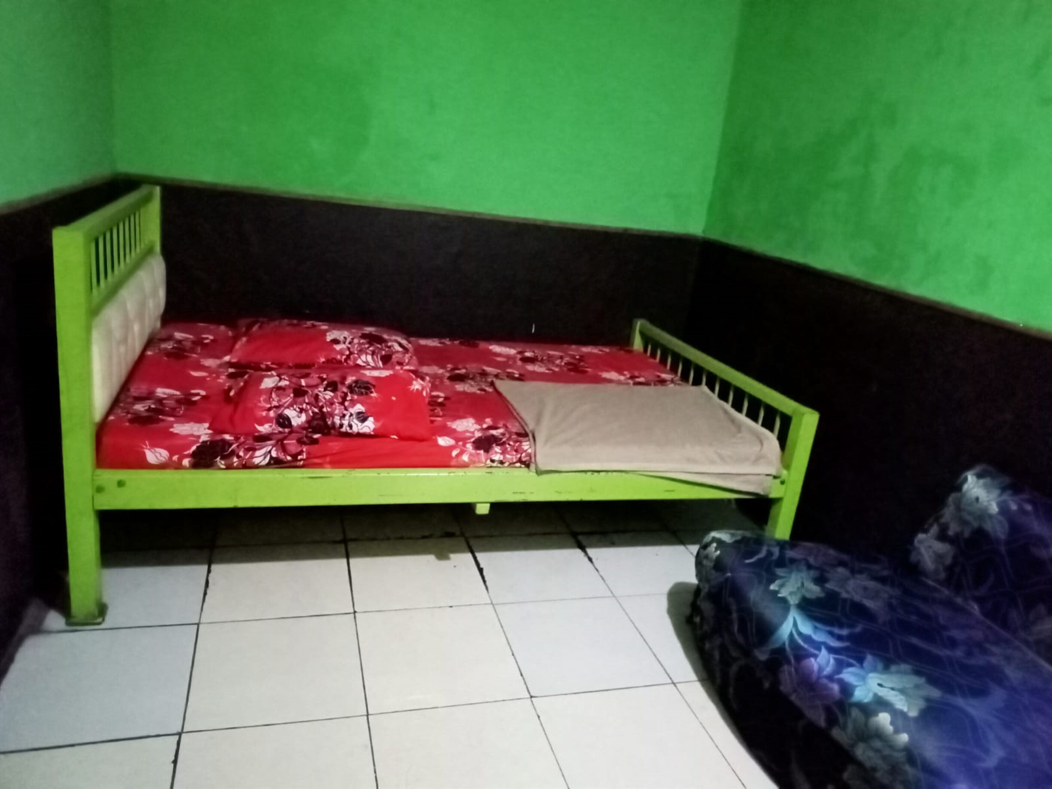 Quarto pequeno com uma cama de solteiro, paredes verdes e chão em azulejos.