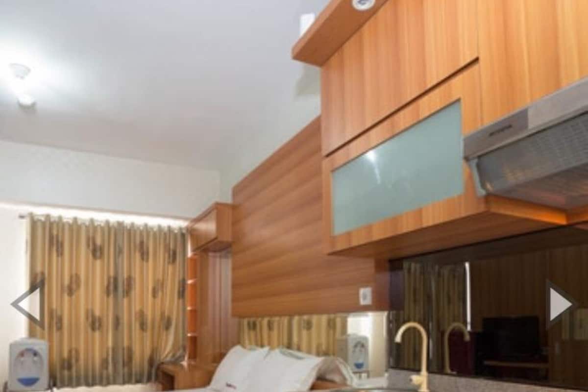 Quarto de hotel compacto com cozinha compacta, uma cama, mesa de cabeceira e janela com cortinas.