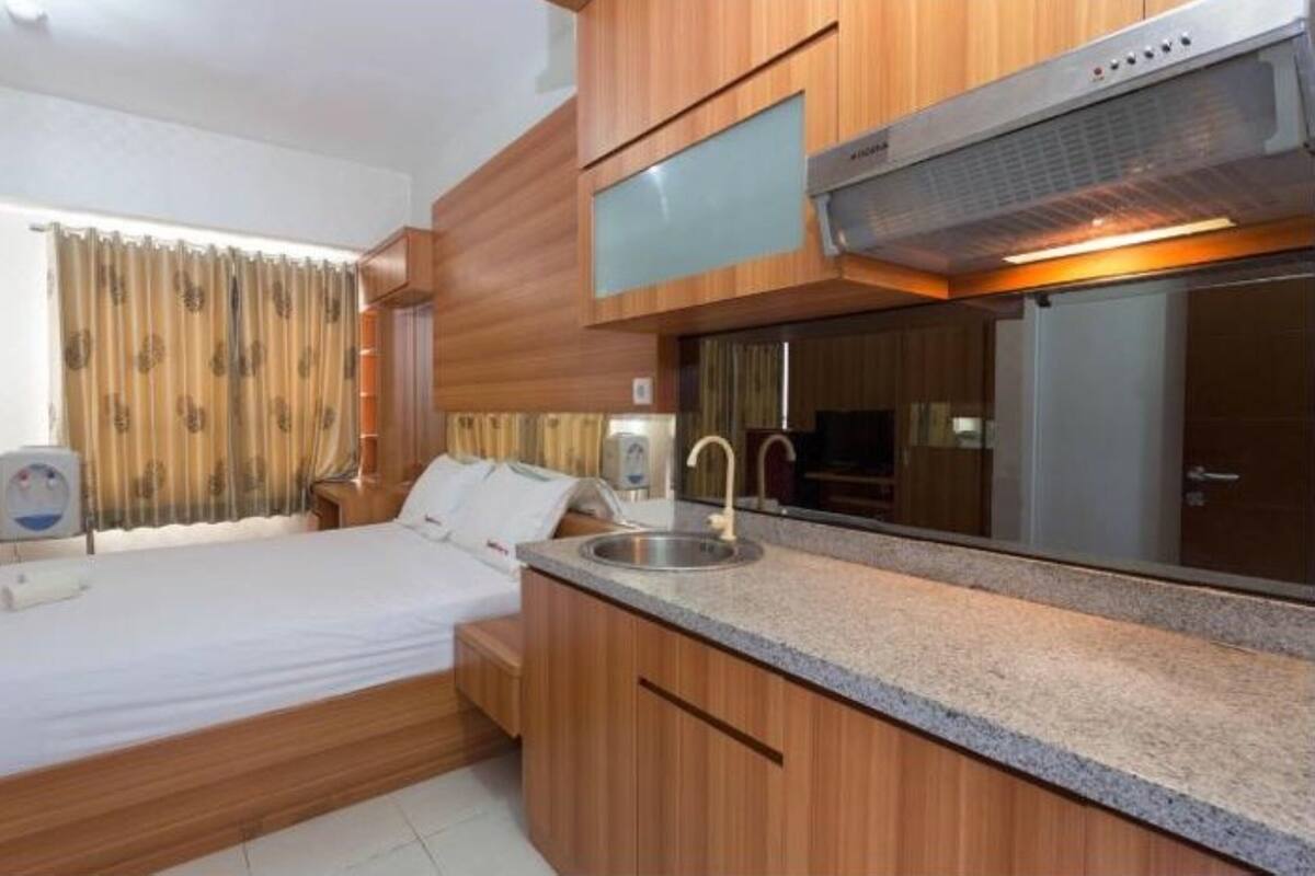 Quarto de hotel compacto com cama, bancada de cozinha, pia e janela com cortinas.
