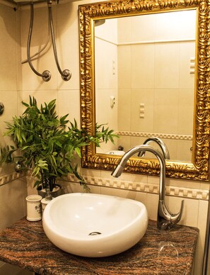 Casa de banho com lavatório branco, espelho com moldura dourada, torneira e planta em vaso.