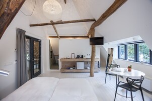 Quarto com uma cama grande, teto de madeira, uma mesa pequena com cadeiras, televisão e janela com vista para o verde.