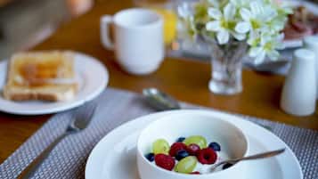 Uma mesa com iogurte e frutas vermelhas, uma chávena e uma fatia de pão torrado.