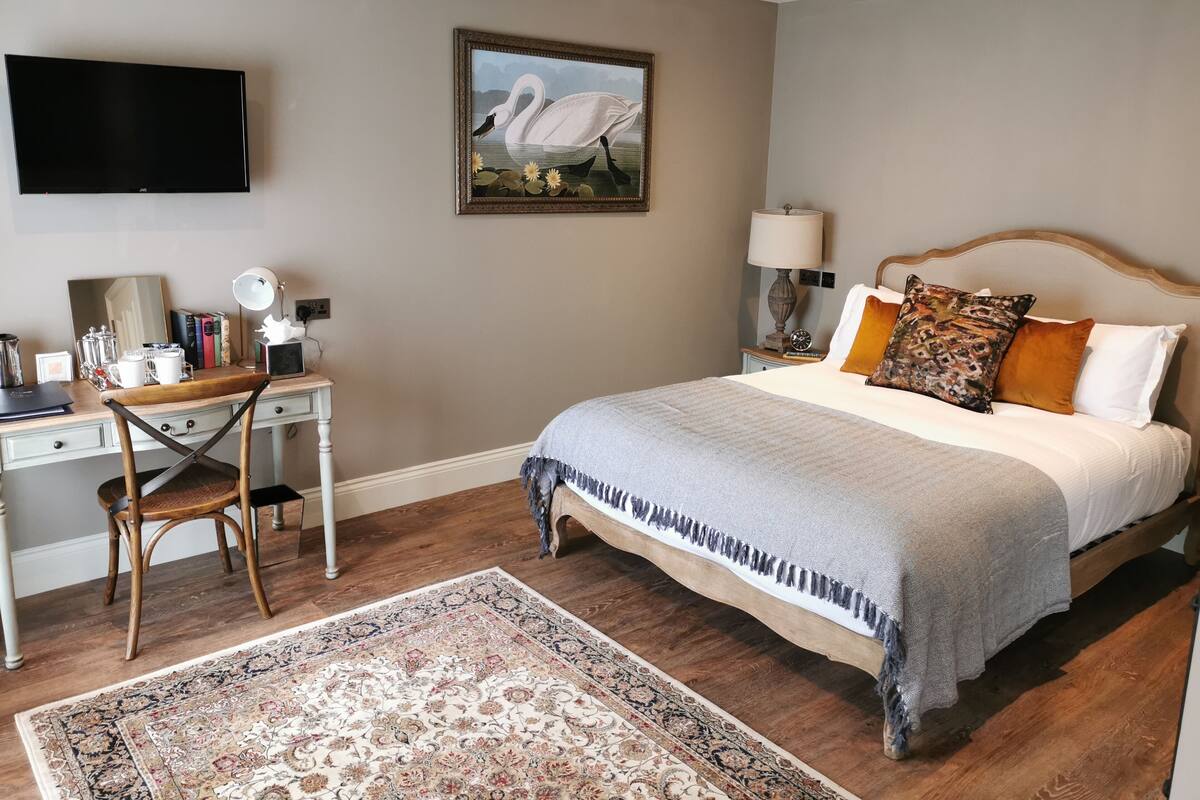 Quarto com cama, escrivaninha, cadeira, televisão e um quadro na parede.