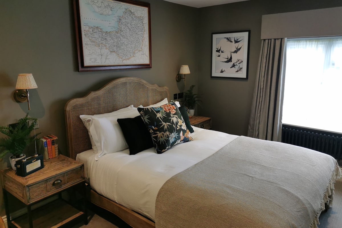 Quarto de hotel bem arrumado com uma cama grande, um mapa na parede, um quadro com pássaros e uma janela com cortinas.