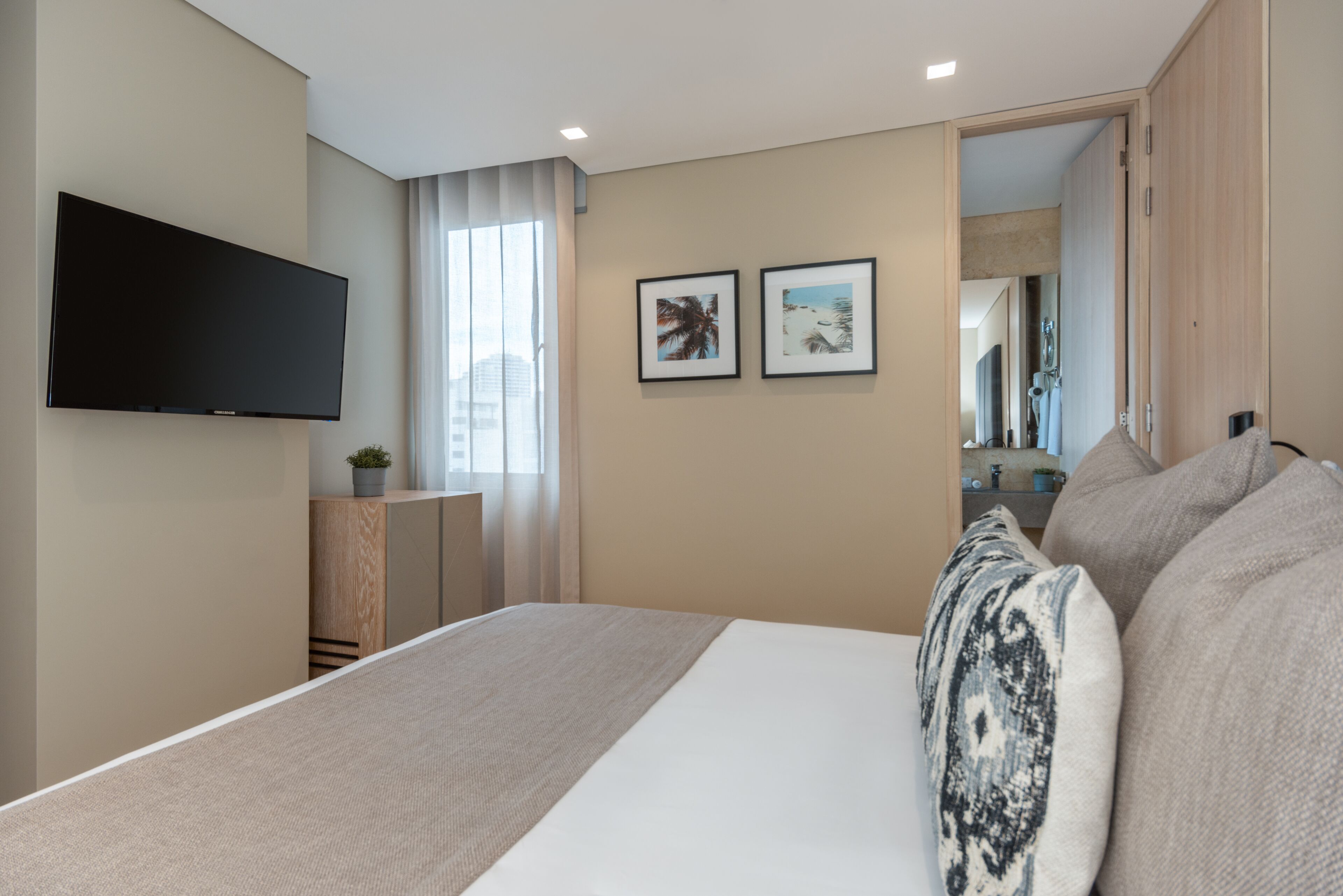 Quarto de hotel moderno com uma cama grande, uma TV de tela plana na parede e duas fotos emolduradas.
